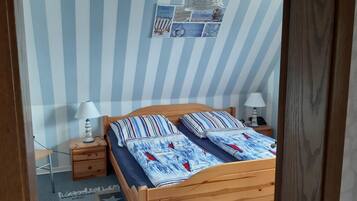 Quarto com parede listrada, cama de madeira com roupa de cama listrada, duas mesas de cabeceira com abajures e uma parede com várias imagens.