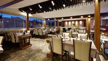 Um restaurante com várias mesas e cadeiras, janelas amplas e design de teto moderno.