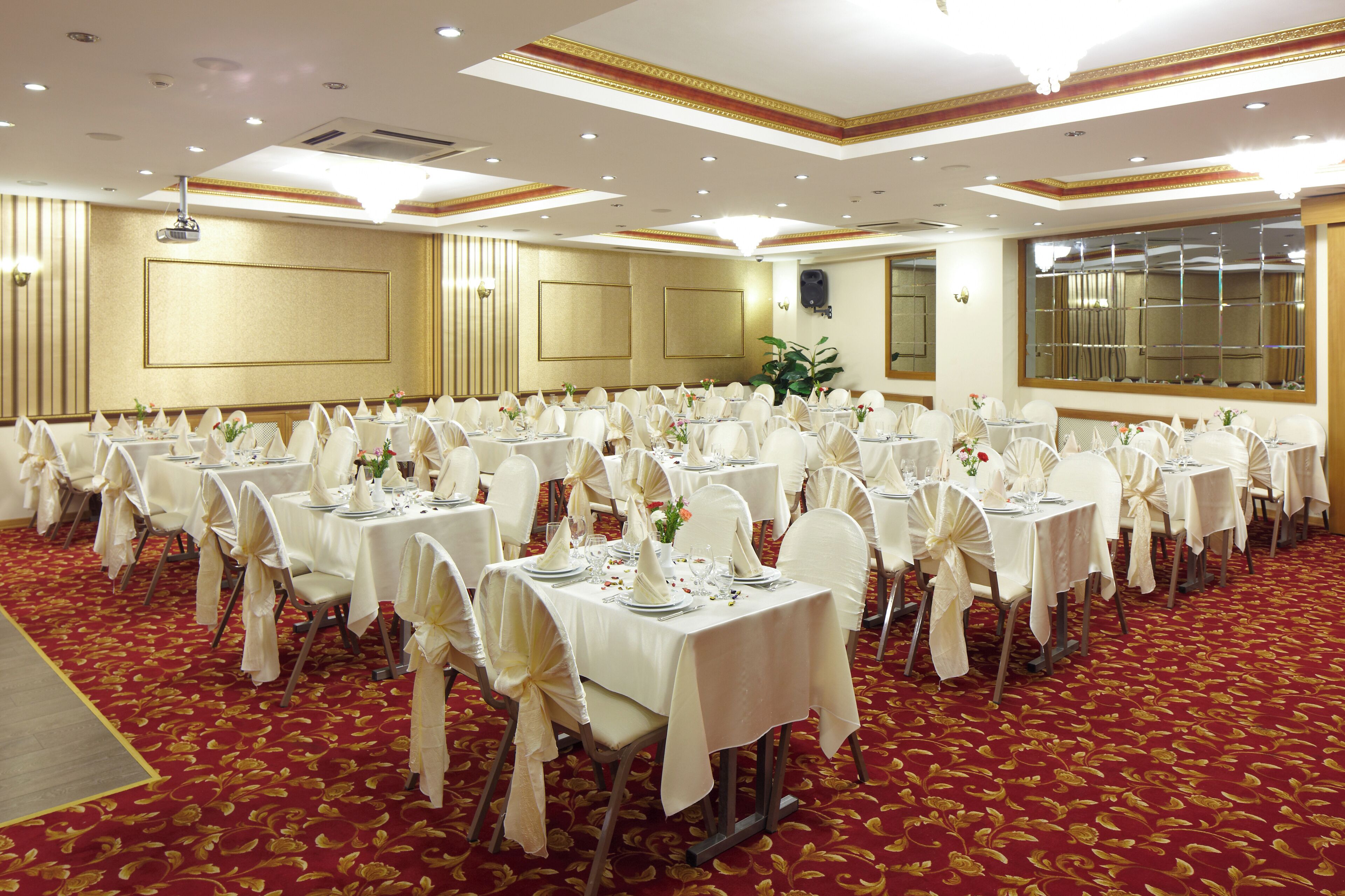 Uma sala de banquetes com várias mesas redondas, cada uma coberta com toalhas brancas e cadeiras, dispostas em fileiras.