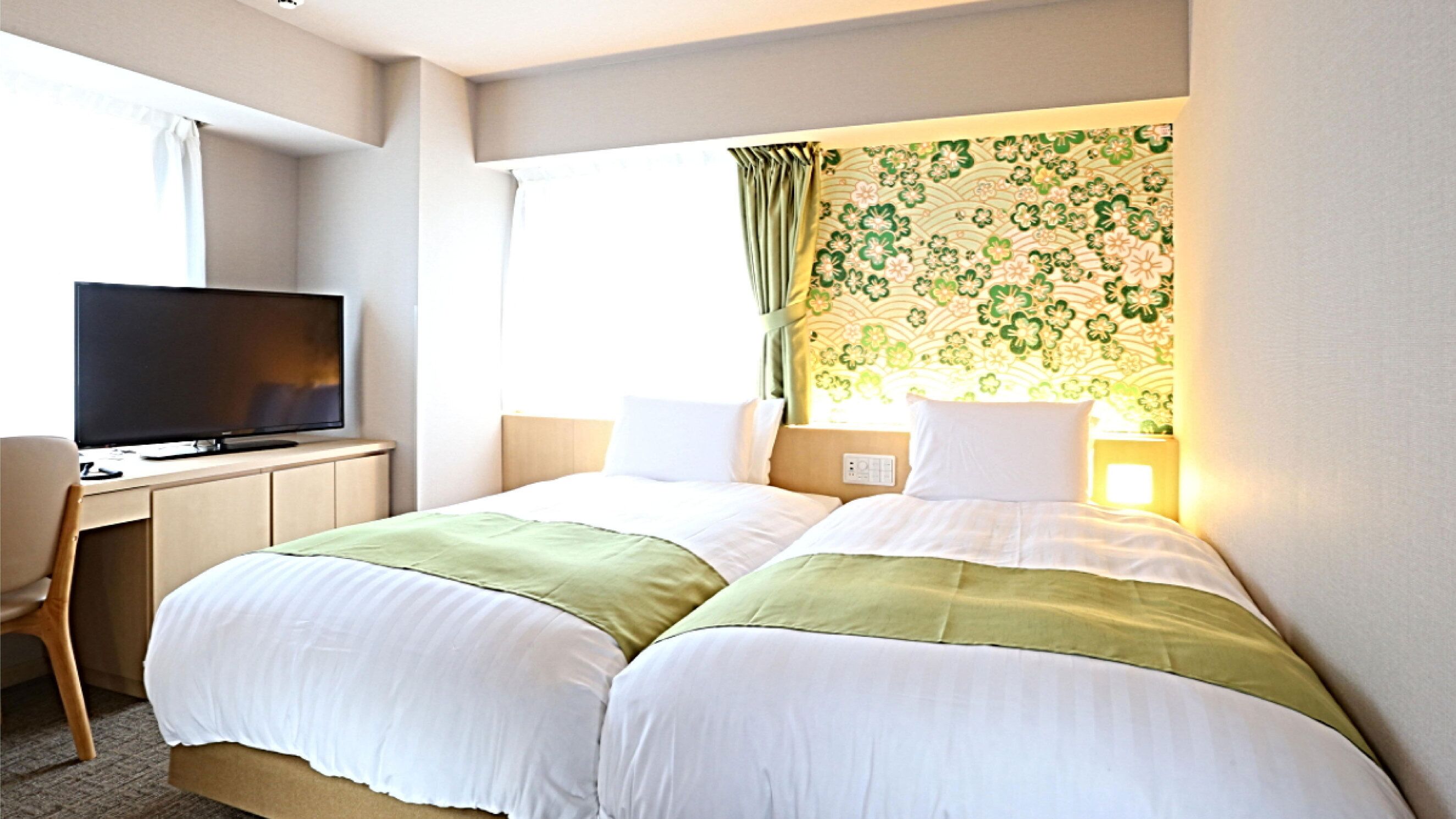 Quarto de hotel com duas camas, uma secretária e uma televisão, além de uma janela com cortinas.