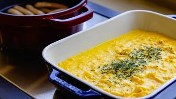 Uma travessa retangular com um prato amarelo e cremoso, possivelmente um gratinado, decorada com ervas, sobre uma bancada escura.