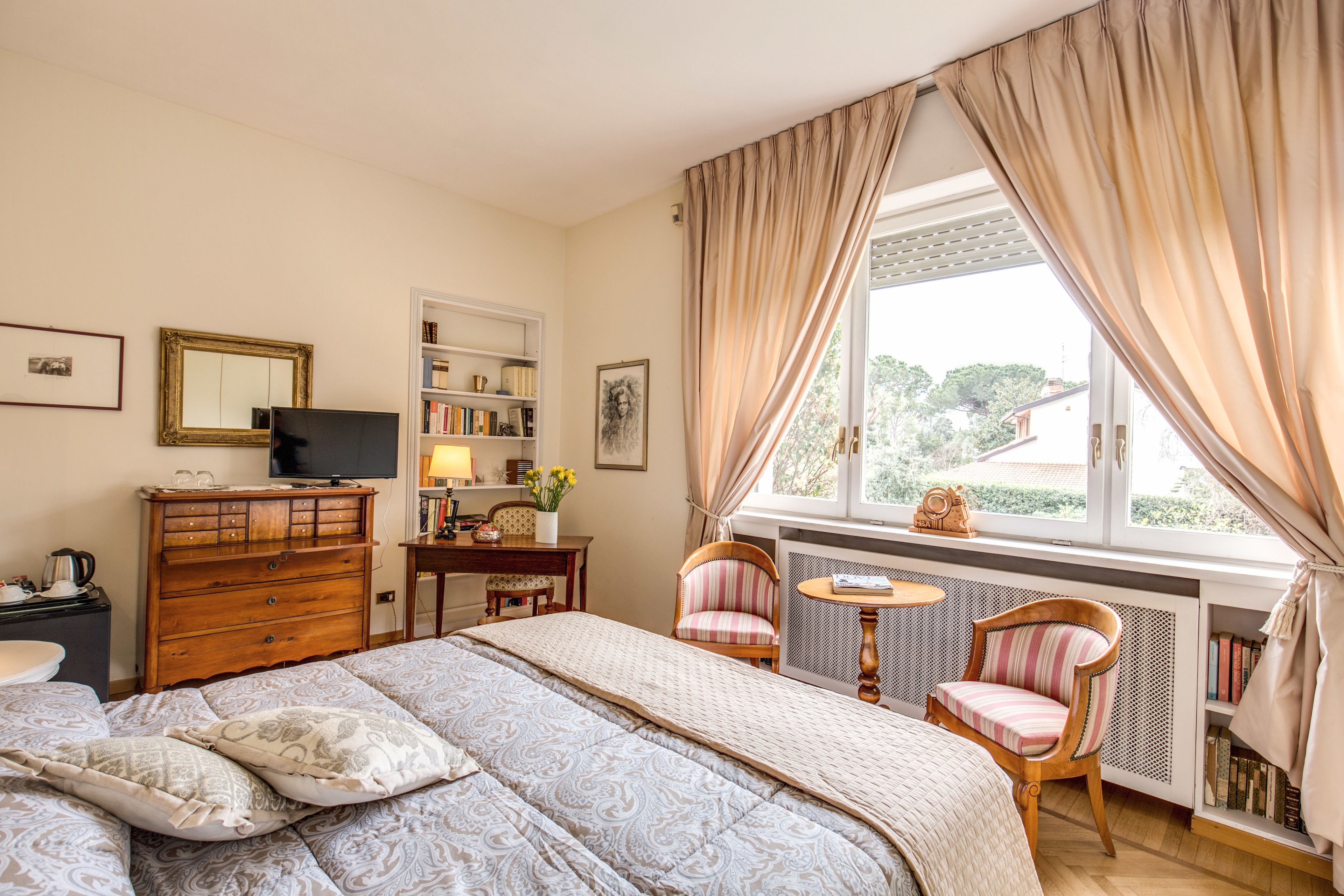 Quarto com cama, cômoda, televisão, cadeira e janela com cortinas.
