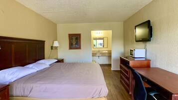 Quarto de hotel com cama grande, escrivaninha, televisão, espelho e banheiro ao fundo.