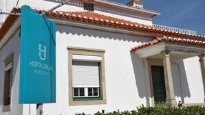 Um edifício branco com telhado de telhas, uma janela com persiana branca e uma porta com painel de vidro decorativo.