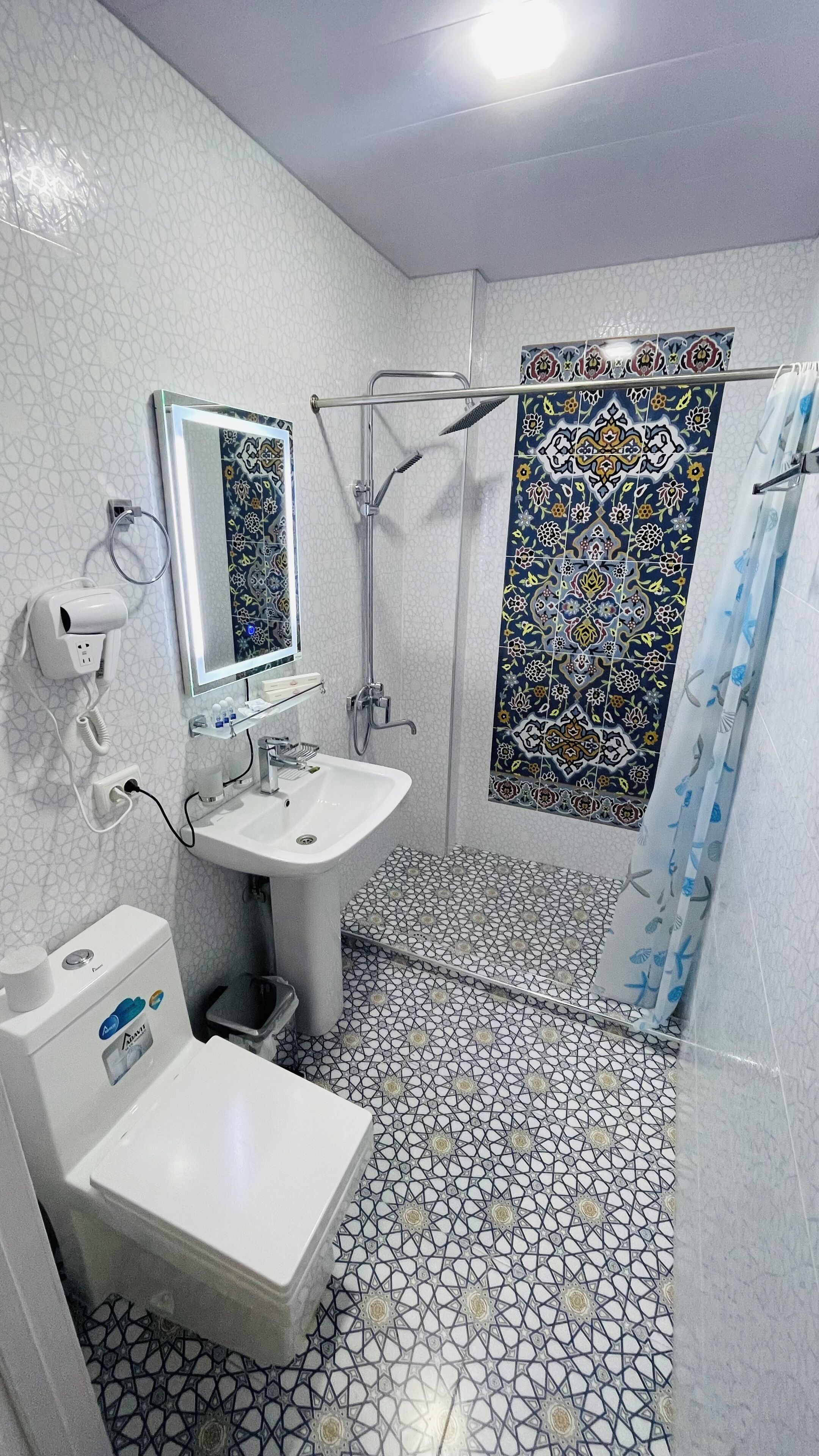 Casa de banho com lavatório, espelho, chuveiro e azulejos estampados.