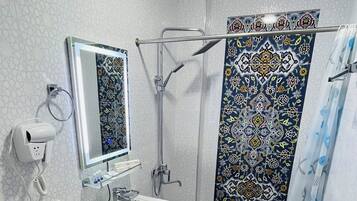 Casa de banho com lavatório, espelho, chuveiro e azulejos estampados.