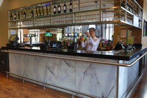 Uma área de bar com bancada de mármore, várias torneiras de cerveja e variedade de garrafas e copos nas prateleiras.