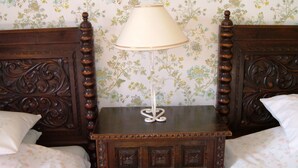 Quarto com duas cabeceiras de madeira, uma mesa de cabeceira com abajur e papel de parede floral.