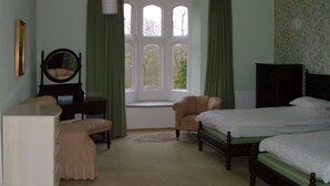 Quarto com uma grande janela, uma cadeira, uma cama, um penteado e um espelho.