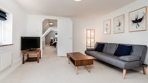 Uma sala de estar moderna com um sofá cinzento, mesa de centro de madeira e uma televisão de tela plana em um suporte.