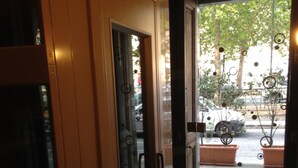 Vista interna de um corredor de hotel com uma porta de vidro que dá para o exterior.
