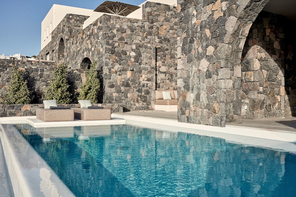Área de piscina com paredes de pedra e piscina azul translúcida.