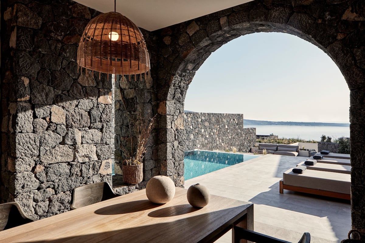 Um quarto com paredes de pedra e uma grande porta arqueada que dá para uma área de piscina.