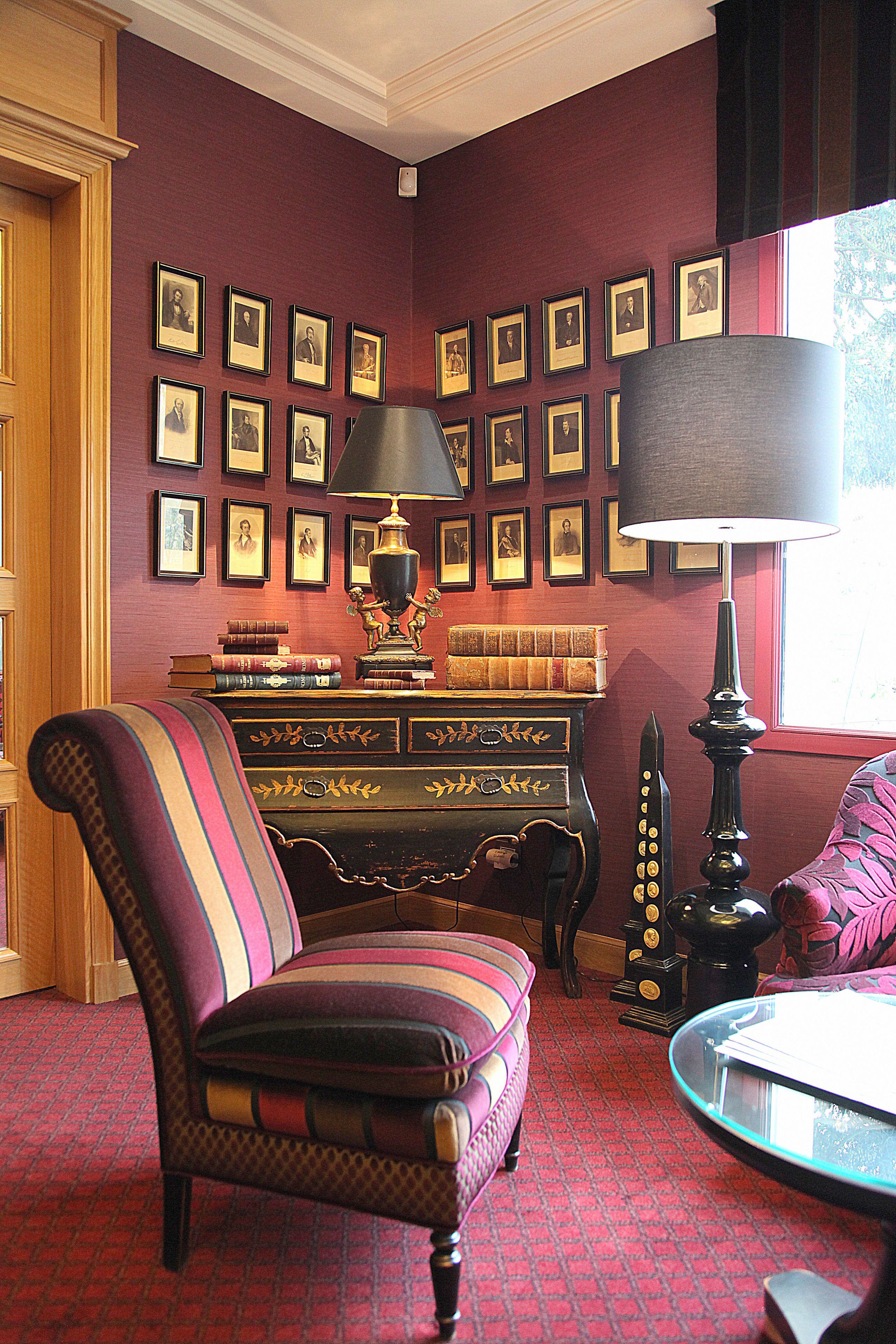 Um quarto com carpete estampado, um armário de madeira, uma cadeira com almofada listrada, uma mesa com abajur e uma parede decorada com quadros.