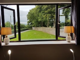 Quarto com uma janela grande de frente para um gramado verde e árvores. Há duas luminárias em cada lado da janela.