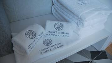 Uma pilha de toalhas brancas com a inscrição 'Guest House Santa Clara' sobre uma superfície branca.