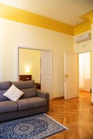 Quarto com sofá, tapete estampado, piso de madeira e porta que dá para outro cômodo.