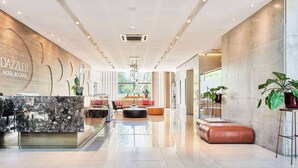 Um hall de hotel moderno com balcão de recepção em mármore, assentos de couro e grandes janelas que proporcionam iluminação natural.