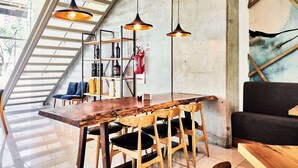 Um interior moderno com uma mesa de jantar de madeira, cadeiras estofadas em preto e iluminação pendente.