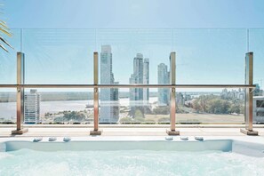 Uma piscina no terraço com guarda-corpo de vidro, oferecendo vista para edifícios altos e um corpo de água.