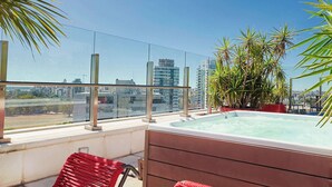 Terraço no telhado com hidromassagem, espreguiçadeiras vermelhas e plantas em vasos.