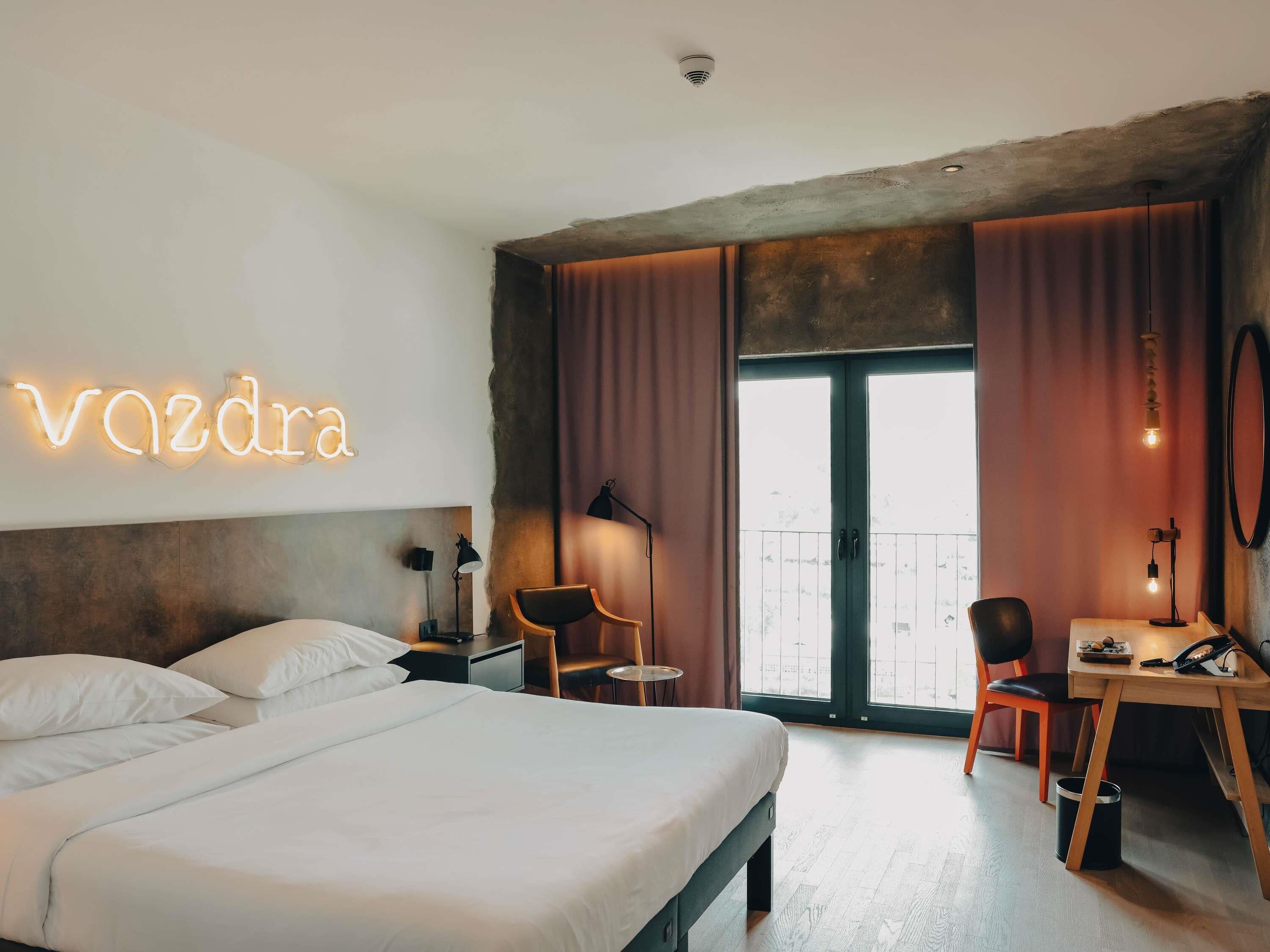 Quarto de hotel com cama, escrivaninha, cadeira e um letreiro luminoso na parede.