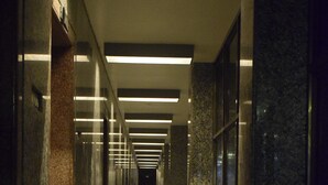 Um corredor com piso espelhado, paredes de vidro e uma série de luminárias no teto.