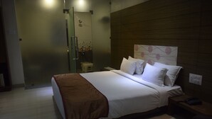 Quarto de hotel moderno com uma cama grande, mesa de cabeceira com telefone e área de chuveiro.
