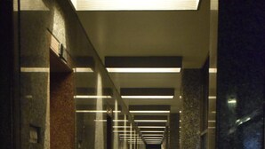 Um corredor com piso refletivo, divisórias de vidro e uma série de colunas uniformemente espaçadas.