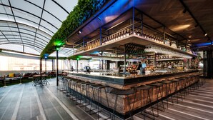 Um bar moderno com teto alto, balcão de madeira e várias áreas de estar.