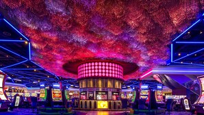 Um casino com várias máquinas de slot, uma área de bar central e um display vibrante no teto.