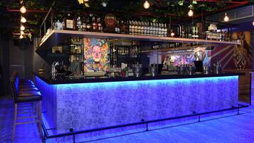 Uma área de bar com balcão revestido de azulejos, prateleiras cheias de garrafas e um mural.