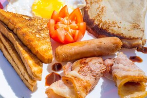 Um prato com torradas, ovo frito, fatia de tomate, salsicha e bacon.
