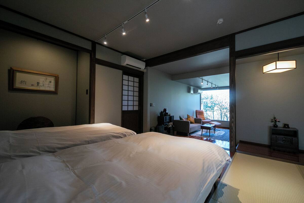 Quarto de hotel com uma cama grande, uma secretária pequena, uma cadeira e vista para o exterior.