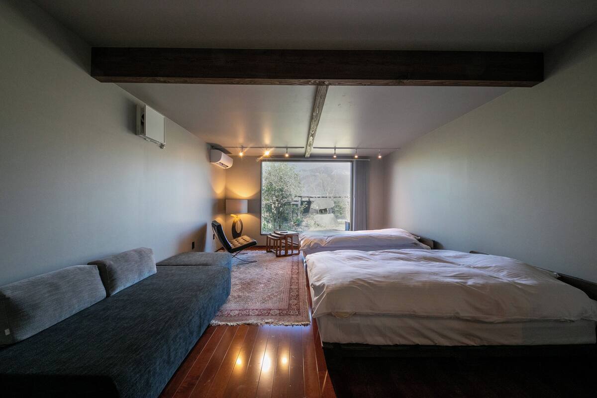 Quarto moderno com uma cama grande, um sofá, uma mesinha e uma janela com vista para o exterior.