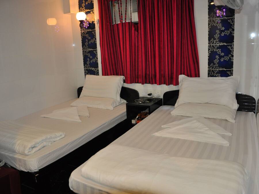 Quarto de hotel com duas camas de solteiro, uma mesa de cabeceira e uma janela com cortinas vermelhas.