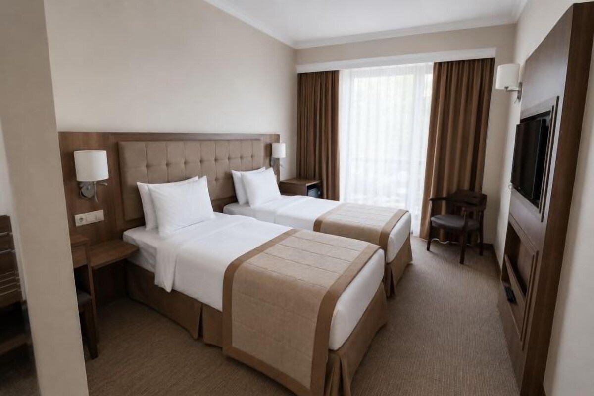 Quarto de hotel com duas camas, televisão, escrivaninha e cadeira.