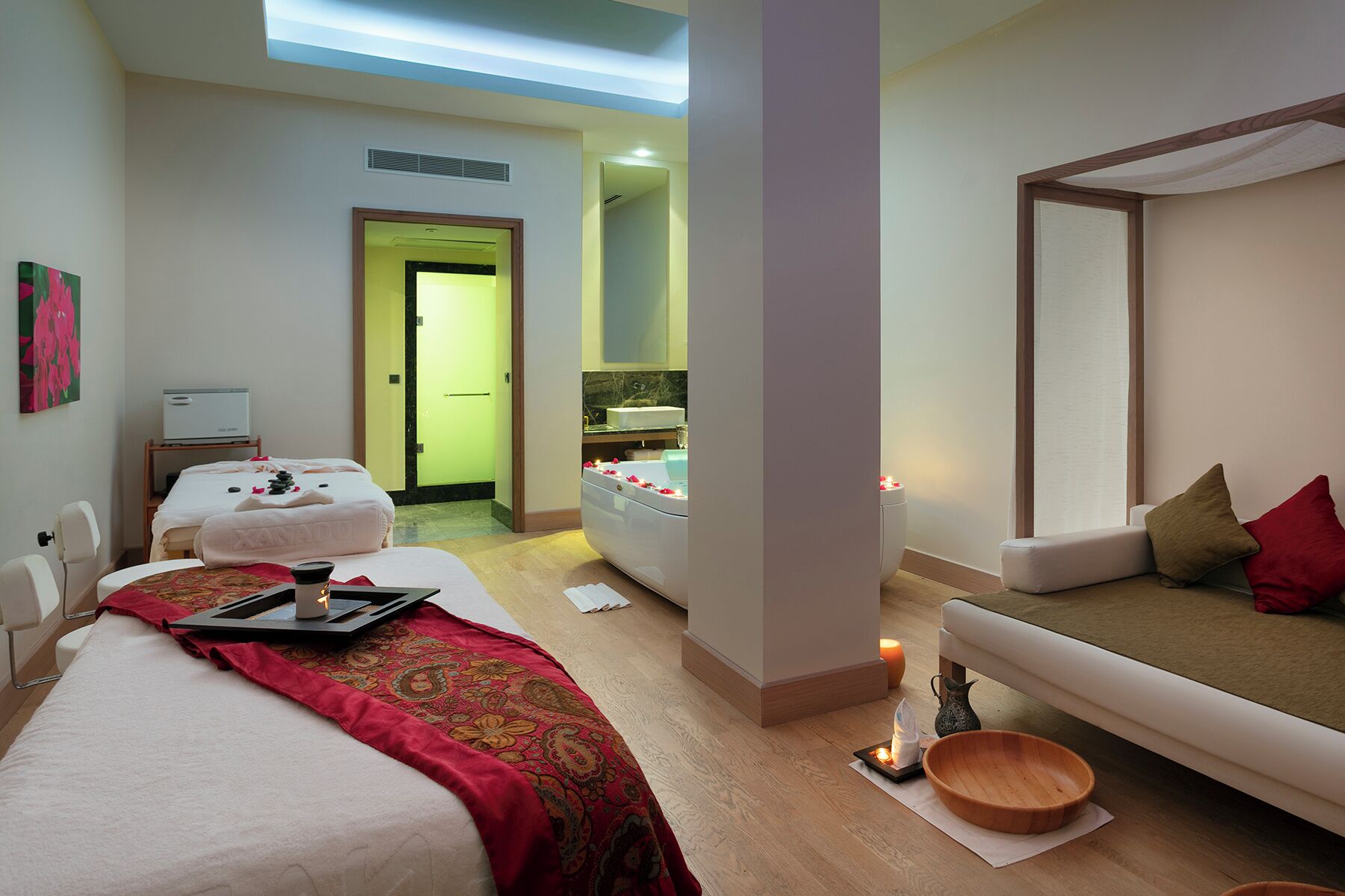 Quarto de hotel com cama, mesa de massagem, área de estar e banheiro com banheira.