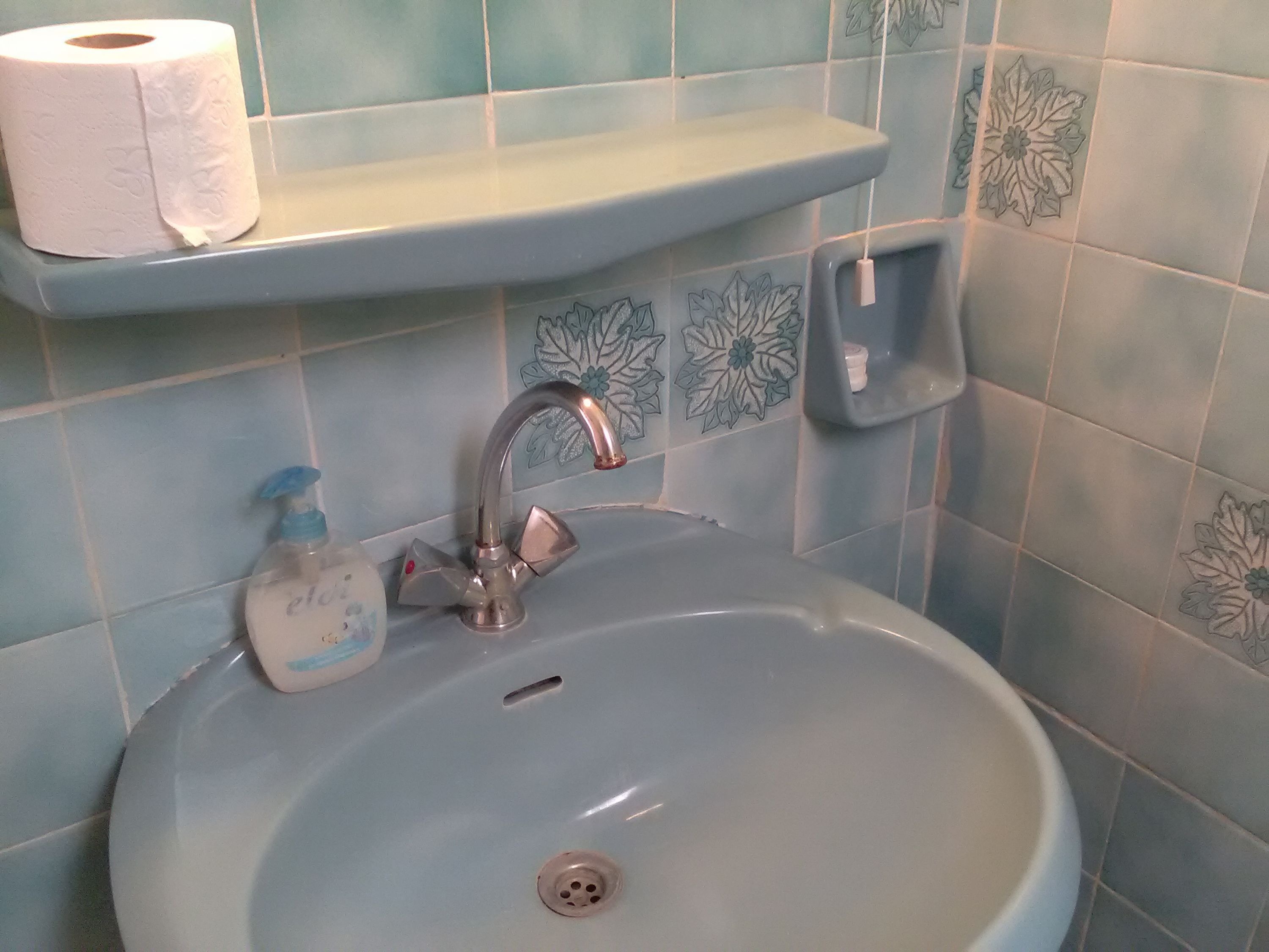 Uma pia de banheiro com uma torneira, um dispensador de sabonete e um suporte para papel higiênico em uma parede com azulejos azuis.