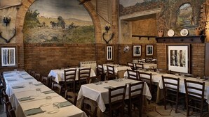 Restaurante com paredes de tijolo, um mural e várias mesas preparadas para refeições.