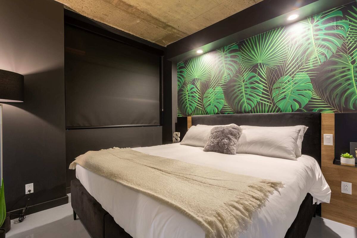 Quarto moderno com cama grande, parede escura e padrão de folha tropical na cabeceira.