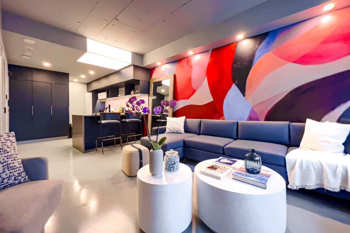Uma sala de estar moderna com um sofá seccional, duas mesas de centro redondas e um mural abstrato e vibrante.