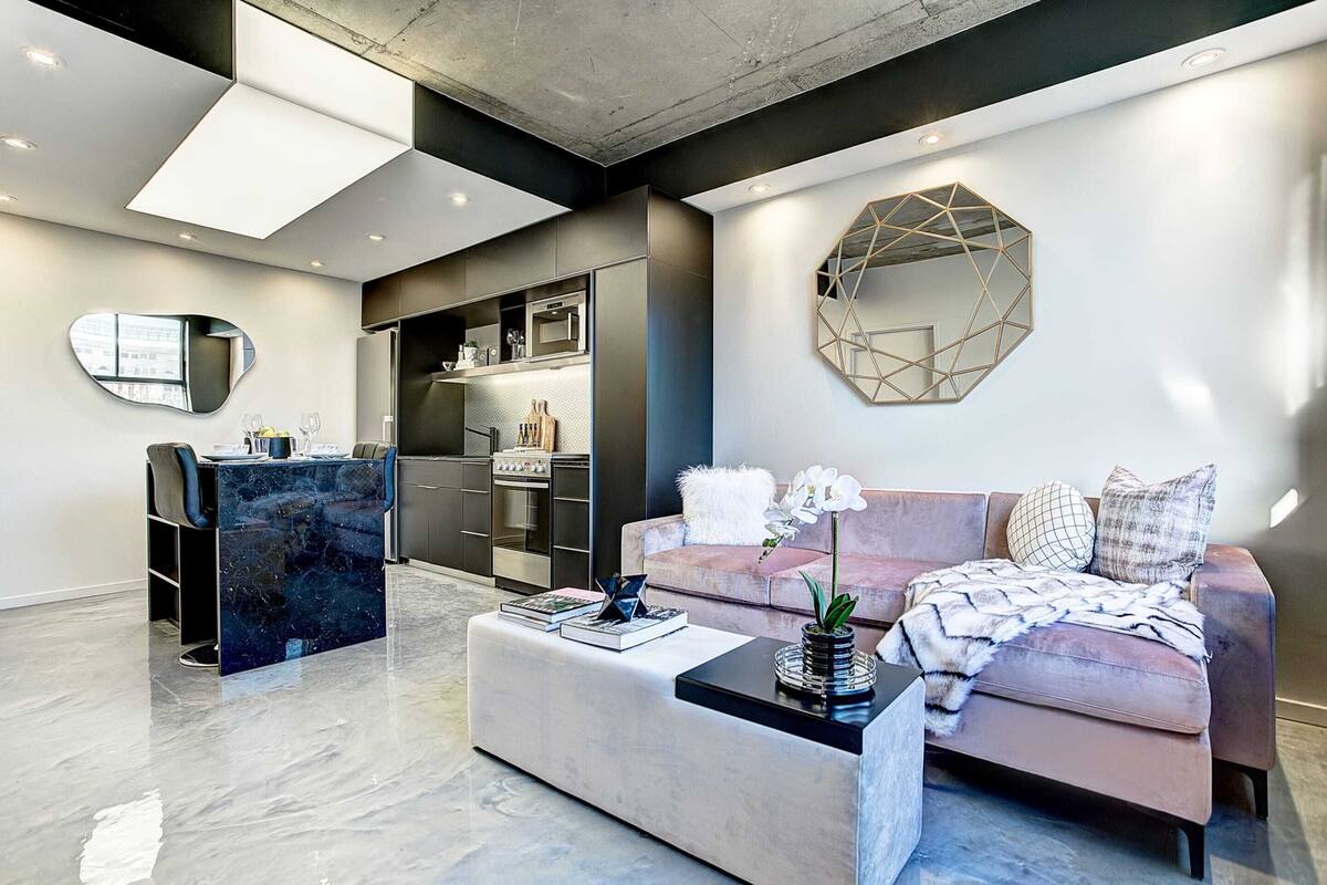 Uma sala de estar moderna com piso de mármore, sofá, mesa de centro e área de cozinha com micro-ondas e armários.