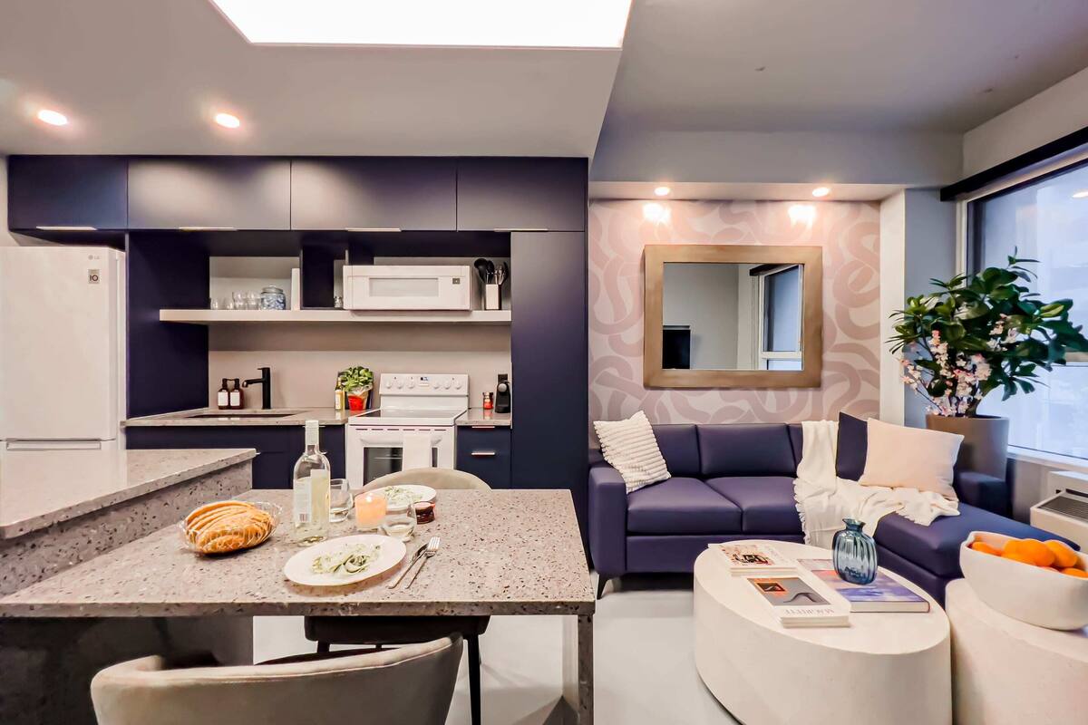 Uma cozinha moderna com eletrodomésticos embutidos, um espaço de refeições com mesa e cadeiras e uma sala de estar com sofá e mesa de centro.