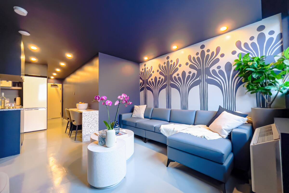 Uma sala de estar moderna com um sofá cinzento, uma mesa de centro branca e uma parede decorativa com padrões semelhantes a árvores.