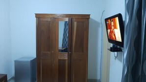 Quarto com guarda-roupa de madeira, televisão na parede e um pequeno alto-falante.
