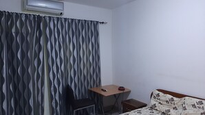 Quarto pequeno com uma cama, uma cadeira, uma mesa e ar condicionado.