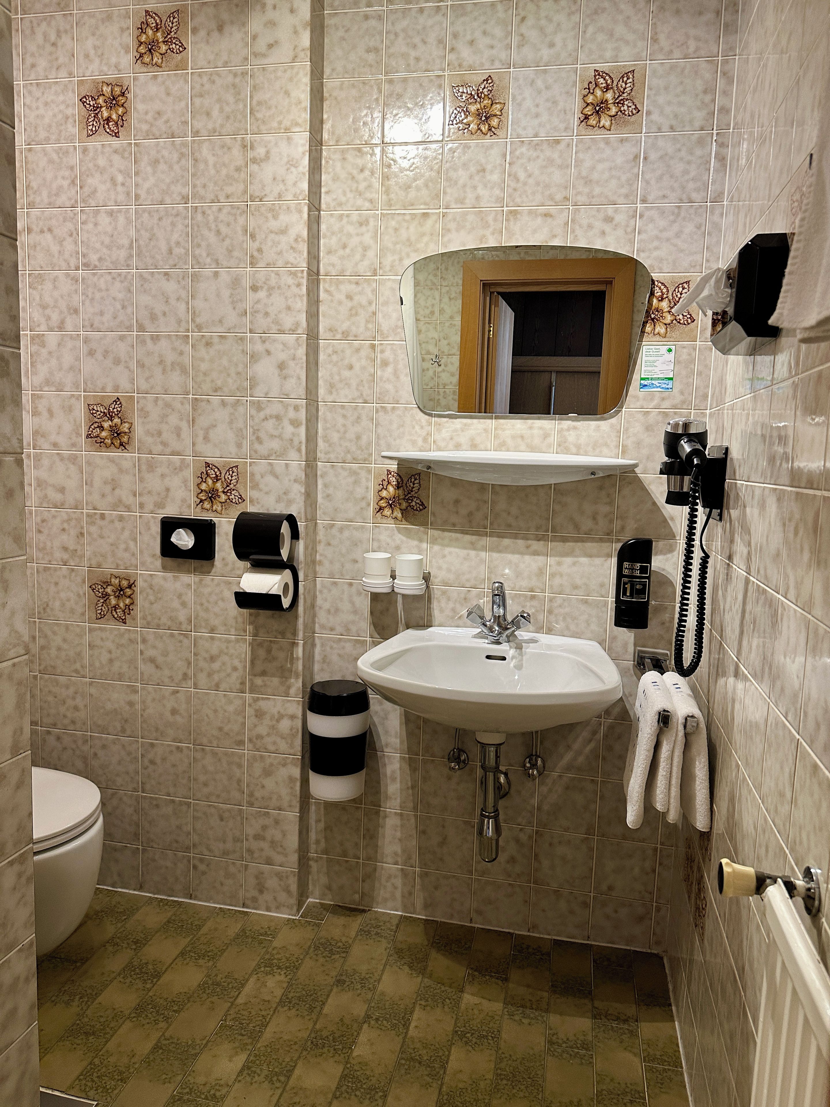 Um banheiro com pia, espelho, porta-toalhas, vaso sanitário e azulejos decorativos.