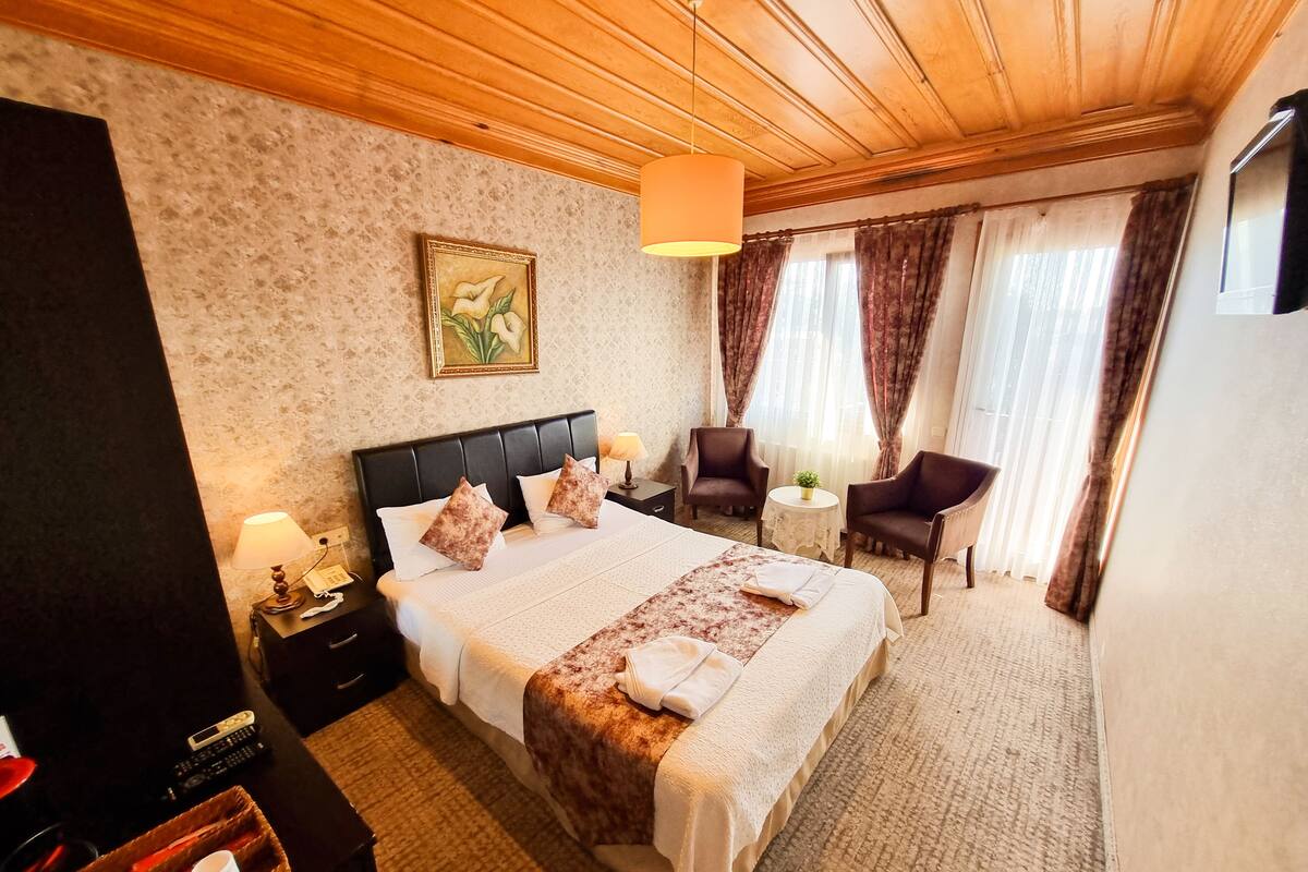 Quarto de hotel com uma cama grande, duas poltronas, uma mesinha de centro com abajur e um quadro na parede.