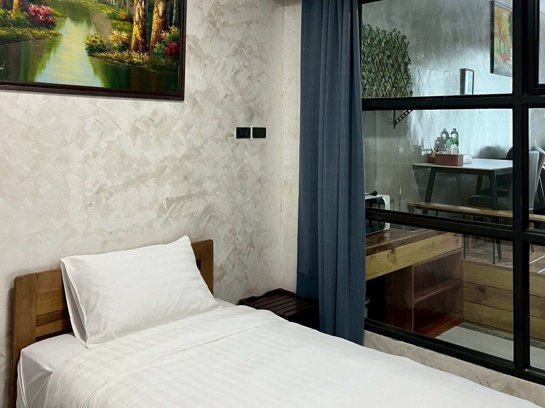 Quarto com cama, janela com vista para uma área de refeições e um quadro na parede.